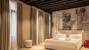 Quarto de hotel moderno com uma cama grande, cortinas bege, um banquinho redondo pequeno e um mural decorativo na parede.