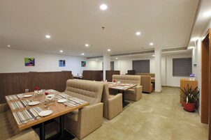 Uma sala de jantar com assentos em cabines e mesas, com disposição de louças e um vaso de planta.