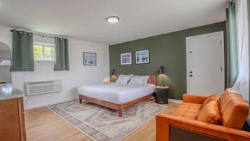 Quarto com cama, luminárias de cabeceira, cômoda, janela com cortinas e porta.