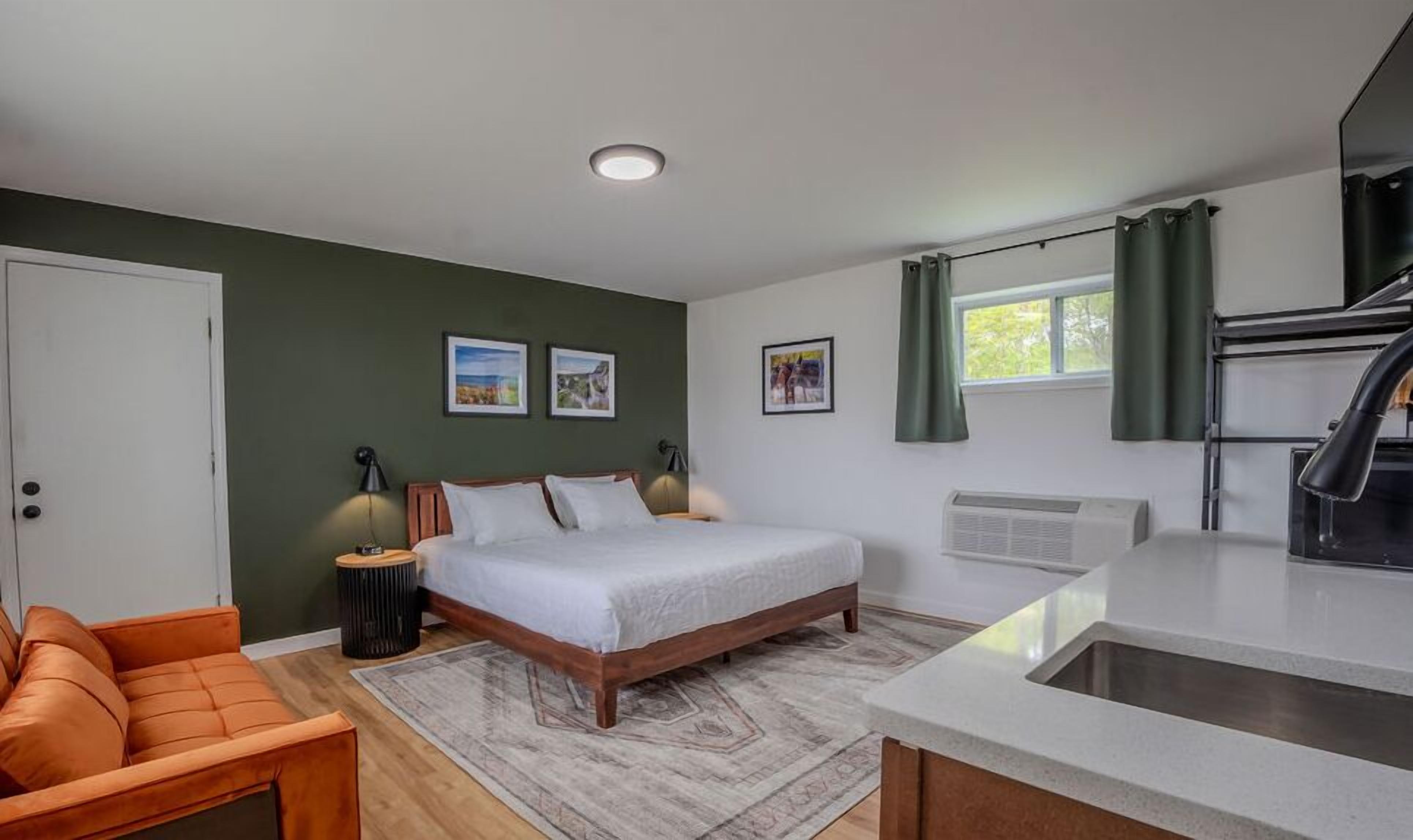 Quarto com cama, mesa de cabeceira, abajur e janela com cortinas.