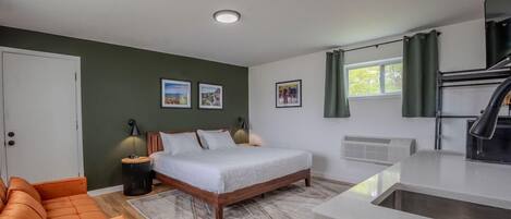 Quarto com cama, mesa de cabeceira, abajur e janela com cortinas.