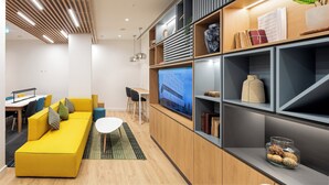 Uma sala de estar moderna com um sofá amarelo, uma TV de tela plana e uma estante de madeira.