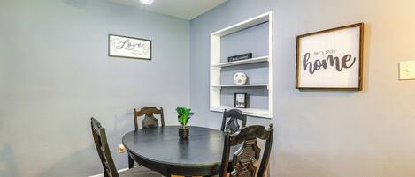Uma sala de jantar com uma mesa redonda, quatro cadeiras, uma planta em vaso e decoração na parede.