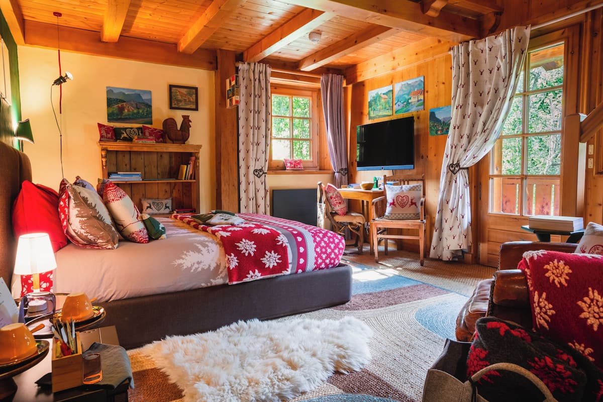Um quarto de cabana de toras aconchegante, com uma cama, uma escrivaninha, uma cadeira, uma televisão e uma estante de livros.