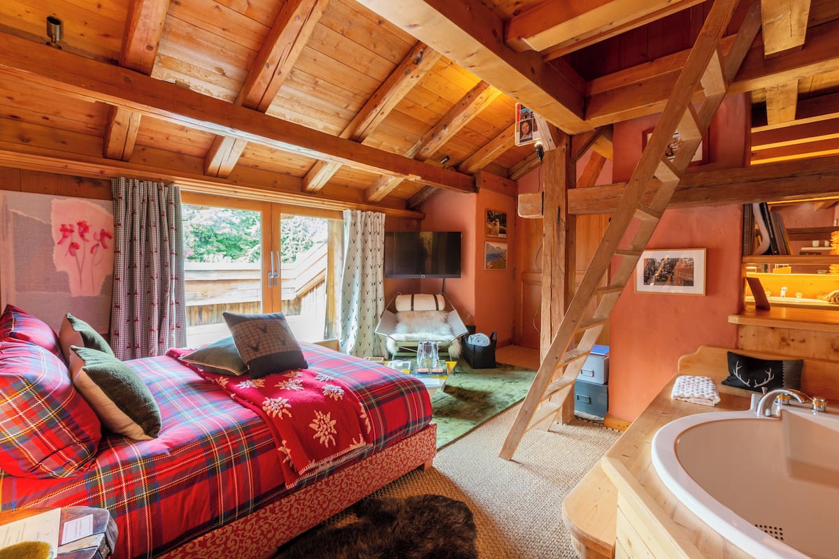 Interior de uma cabana de madeira com uma cama, um banheiro com uma banheira de madeira e uma escada.