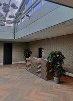 Um hall amplo com um balcão de recepção moderno, uma janela grande e um piso com padrão herringbone.