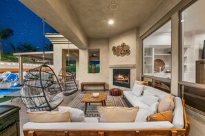 Uma área de estar ao ar livre ampla, com piscina, espreguiçadeiras, um sofá e uma lareira.