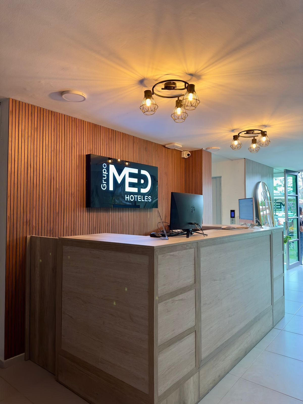 Uma receção de hotel com parede de painel de madeira, uma televisão e uma luminária moderna.
