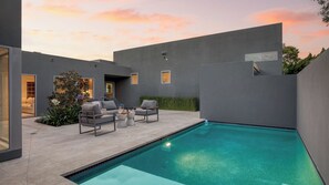 Uma área de piscina moderna ao ar livre, com design minimalista, incluindo piscina, área de estar e um edifício com grandes janelas.