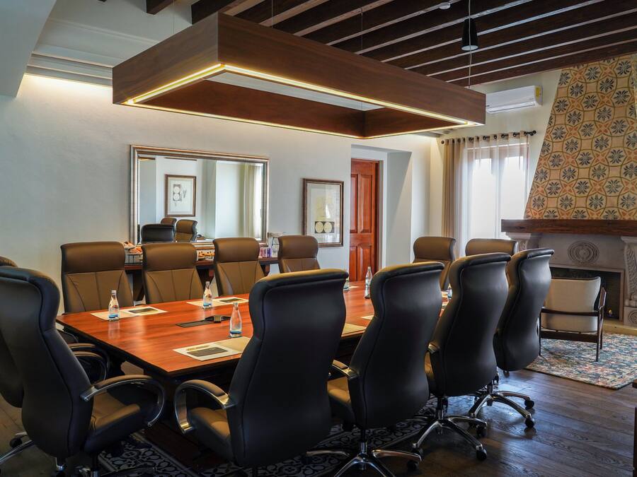 Uma sala de conferências com mesa de madeira, cadeiras pretas e lareira.