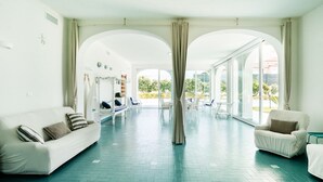 Uma sala de estar ampla com um sofá branco, um espaço de estar coberto e vista através de grandes janelas.