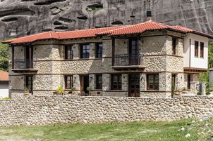 Um edifício de pedra com telhado em tijolos vermelhos, várias varandas e um muro de pedra à frente.