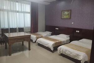 Quarto de hotel com duas camas de solteiro, uma mesa de madeira e uma janela com cortinas finas.