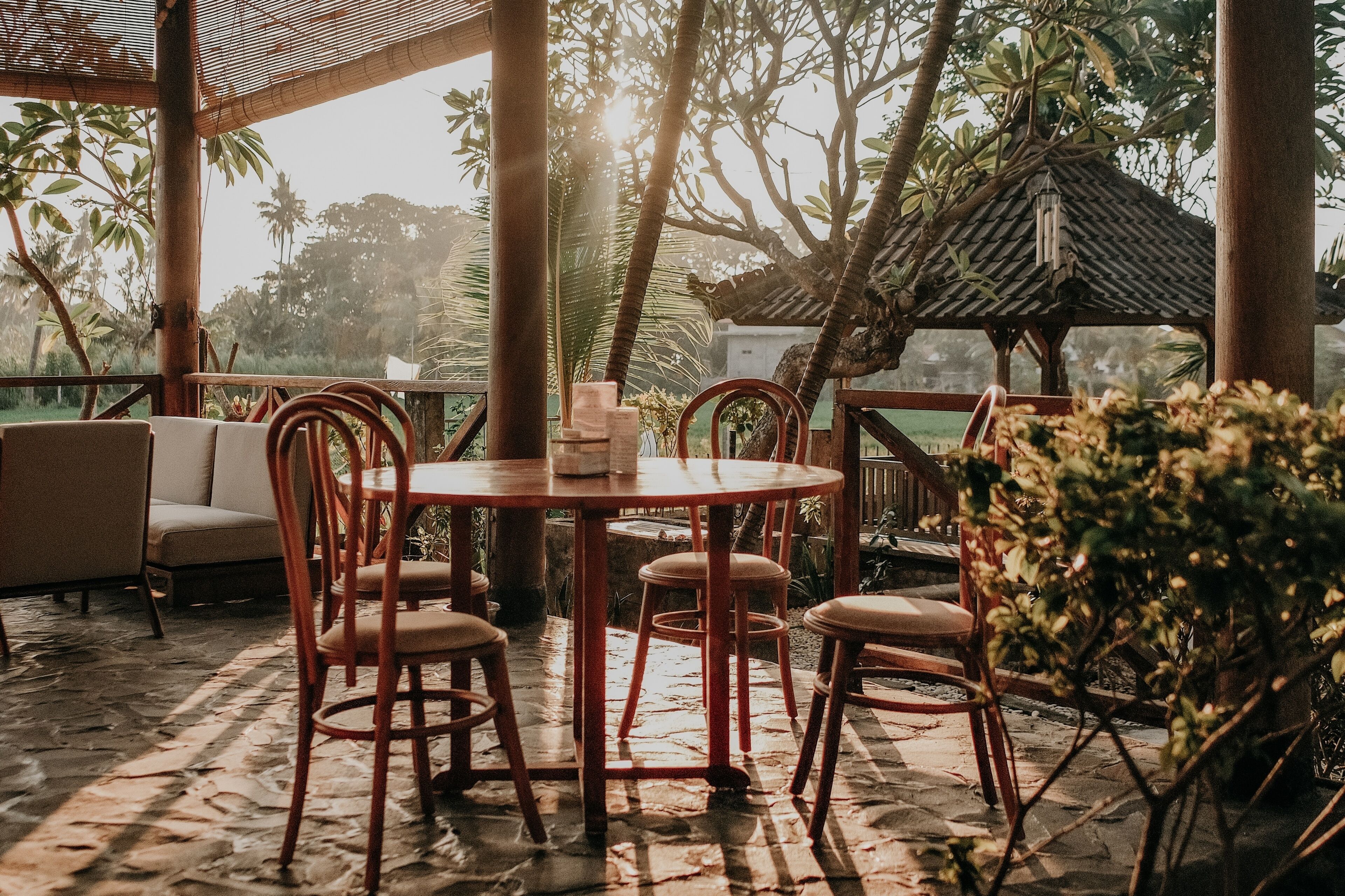 Uma área externa com mesas e cadeiras redondas, cercada por árvores e um gazebo.