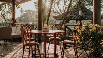 Uma área externa com mesas e cadeiras redondas, cercada por árvores e um gazebo.