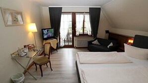 Quarto de hotel com cama, escrivaninha com computador, cadeira, televisão e janela com cortinas.