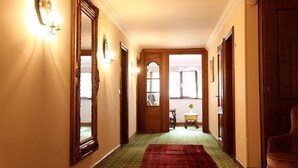 Um corredor com carpete vermelho, portas de madeira e um espelho à esquerda.