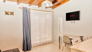 Quarto moderno com mesa de jantar, cadeiras, sofá, televisão na parede e cortina.