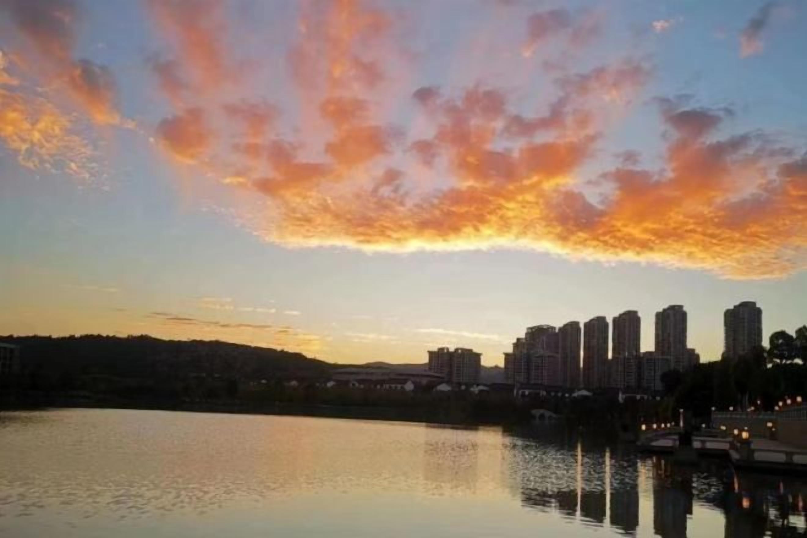 Um lago tranquilo com o skyline de uma cidade ao fundo durante o pôr do sol.