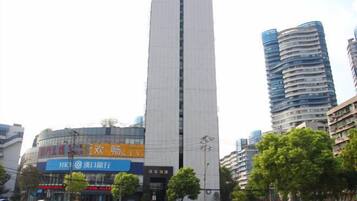 Um edifício alto com design moderno, cercado por outros arranha-céus e uma rua arborizada.