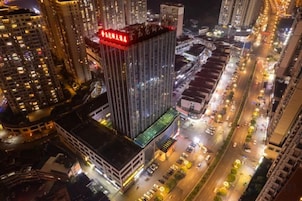 Um edifício alto com letreiros iluminados, cercado por uma movimentada rua urbana à noite.