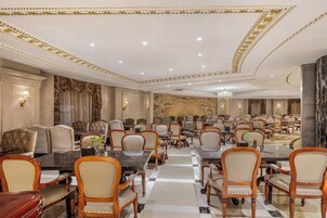 Uma sala de jantar formal com várias mesas e cadeiras, design de teto elegante e um candelabro.