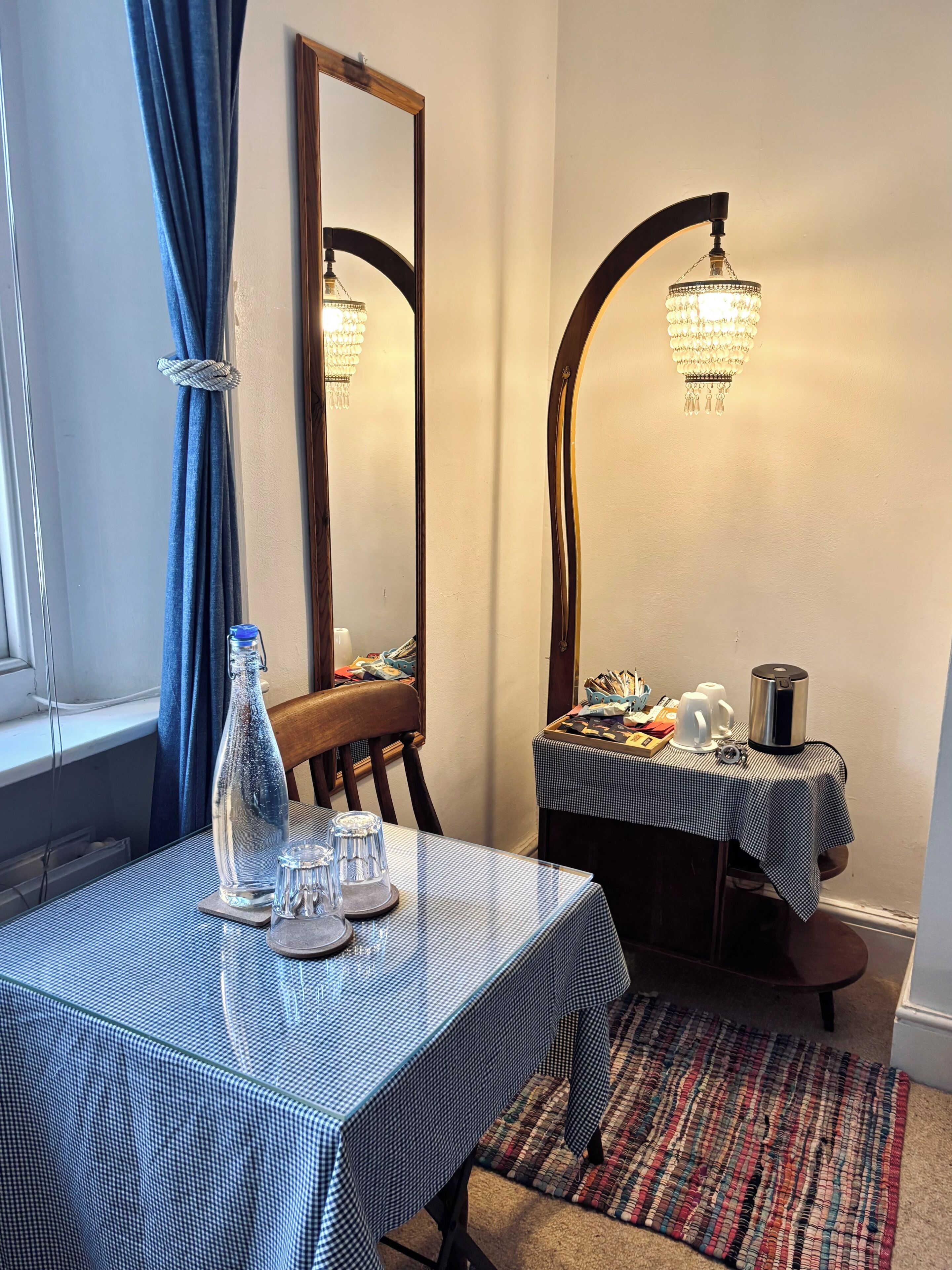 Quarto com mesa posta para refeições, espelho, lustre e cafeteira.