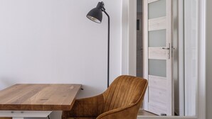 Uma mesa de jantar de madeira com uma cadeira, um abajur e uma parede branca com uma porta e uma janela.