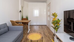 Uma sala de estar moderna com um sofá cinzento, mesa de jantar de madeira e uma TV em um móvel branco.