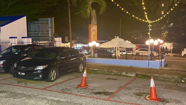 Uma área de estacionamento com carros, uma palmeira e luzes de Natal.