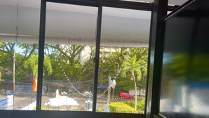 Vista da janela com moldura de metal, mostrando uma rua com carros estacionados e árvores.