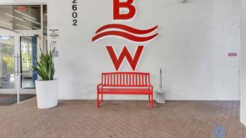 Entrada de um edifício com um banco vermelho, uma planta em vaso e um painel de sinalização de alarme de incêndio.