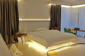 Quarto de hotel com cama, mesa de cabeceira, cadeira e cortinas.