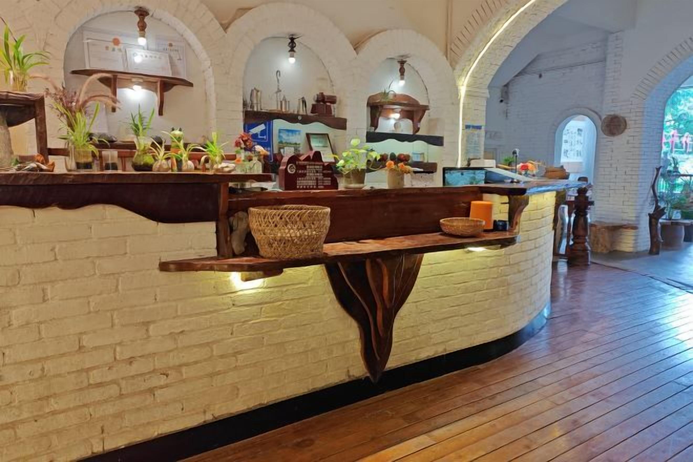 Uma área de bar com balcão de tijolos, banquetas de madeira e plantas em vasos.