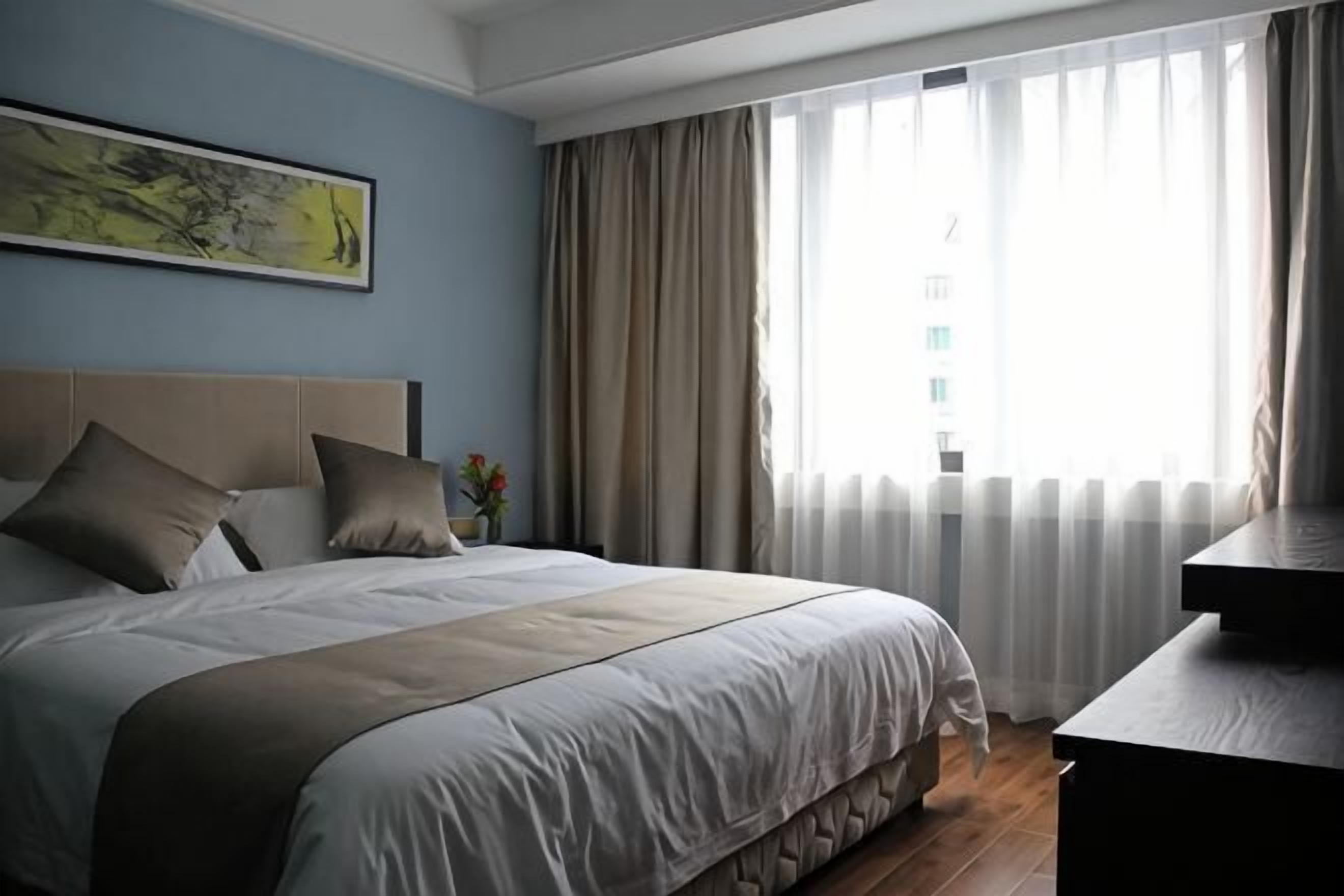 Quarto de hotel com uma cama grande, uma escrivaninha e janela com cortinas.