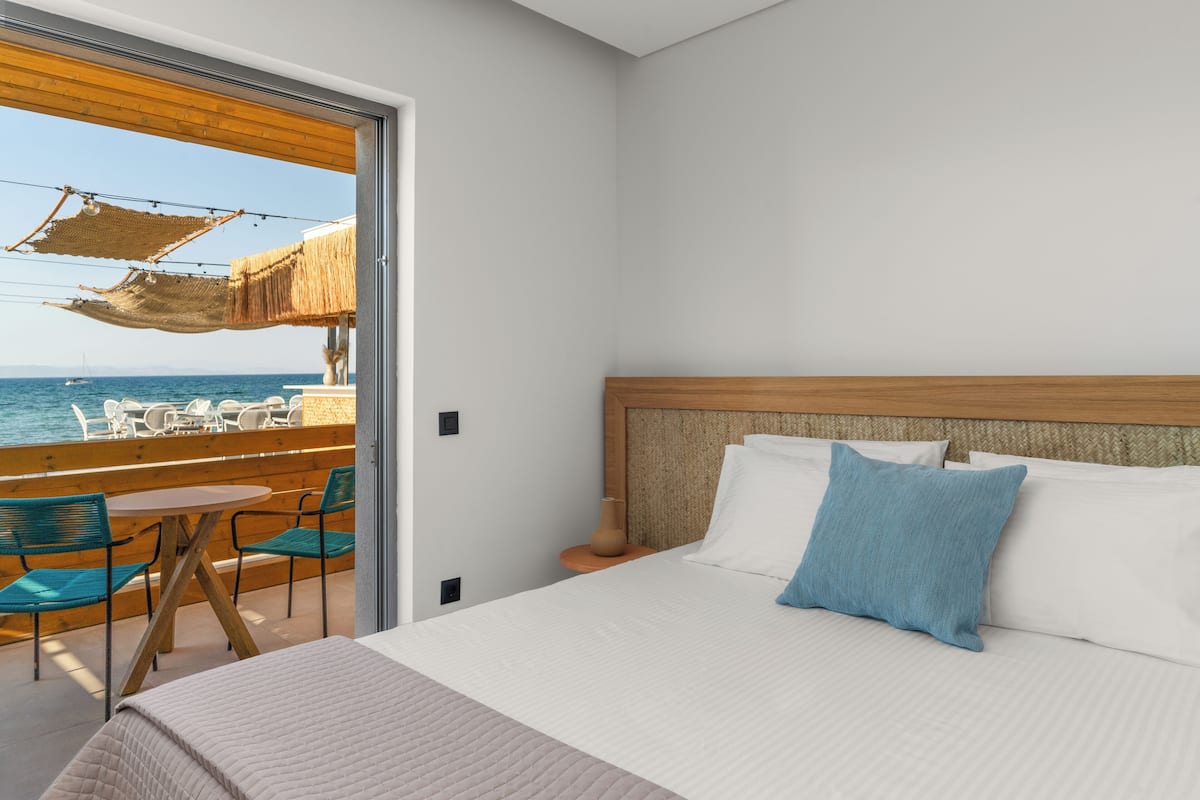 Quarto de hotel com cama, varanda com cadeiras e mesa, e vista para o mar.