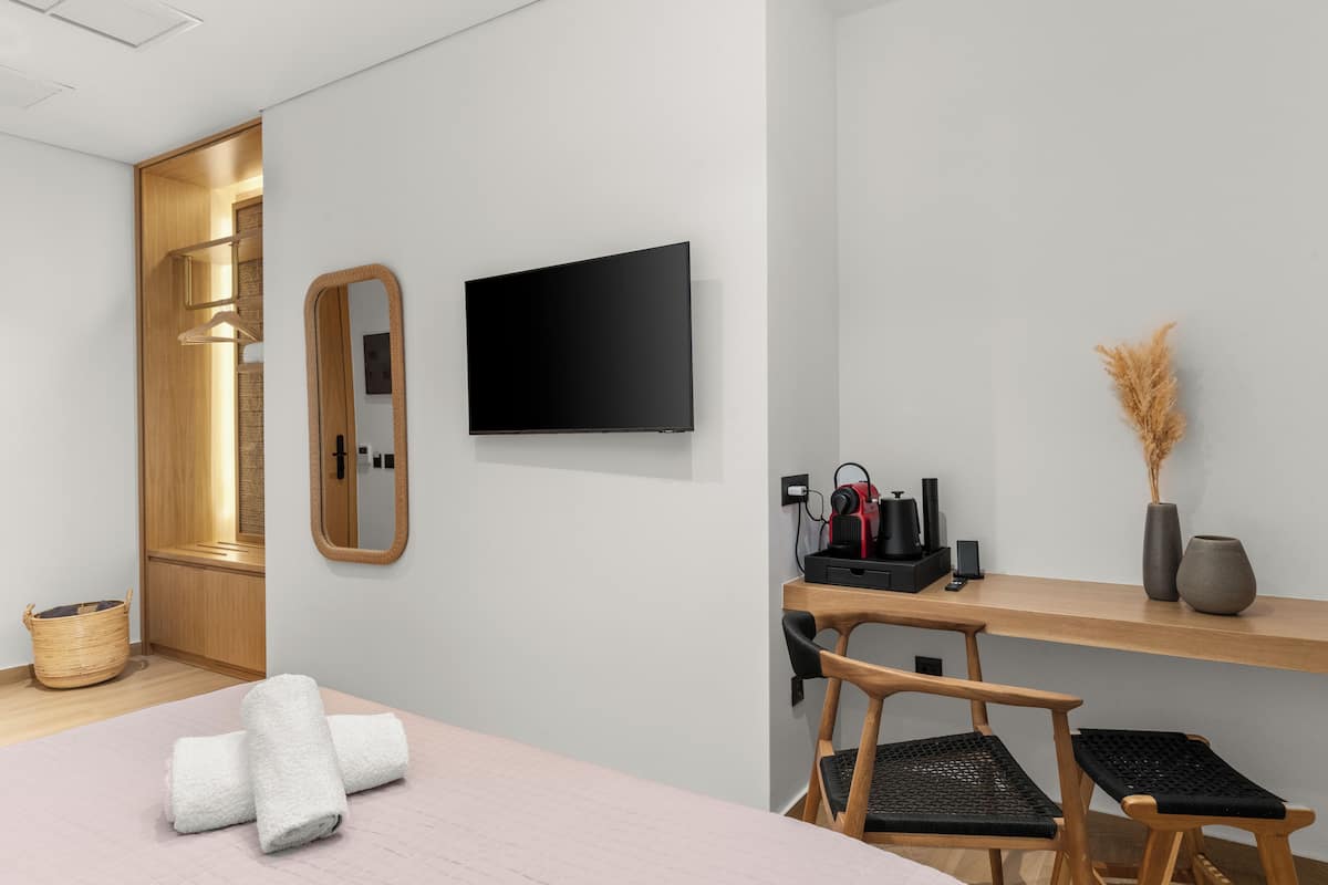 Quarto de hotel moderno com guarda-roupa de madeira, televisão de ecrã plano, secretária com computador e cama com toalhas.