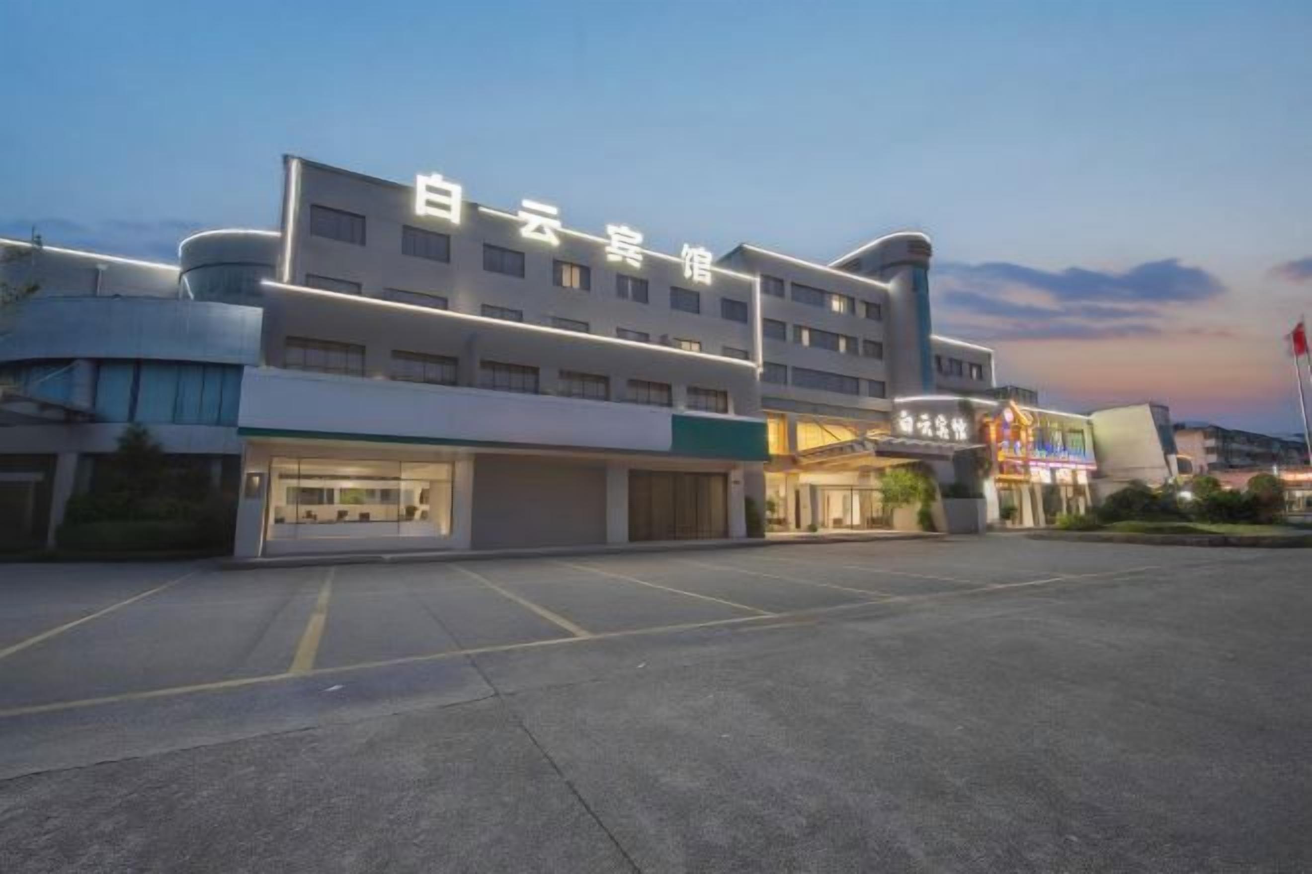 Um hotel moderno com uma placa chamativa, vários andares e um estacionamento.