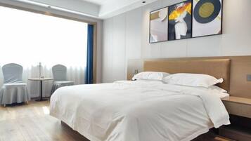 Quarto de hotel moderno com cama grande, mesa de cabeceira, cadeira e vista para a cidade.
