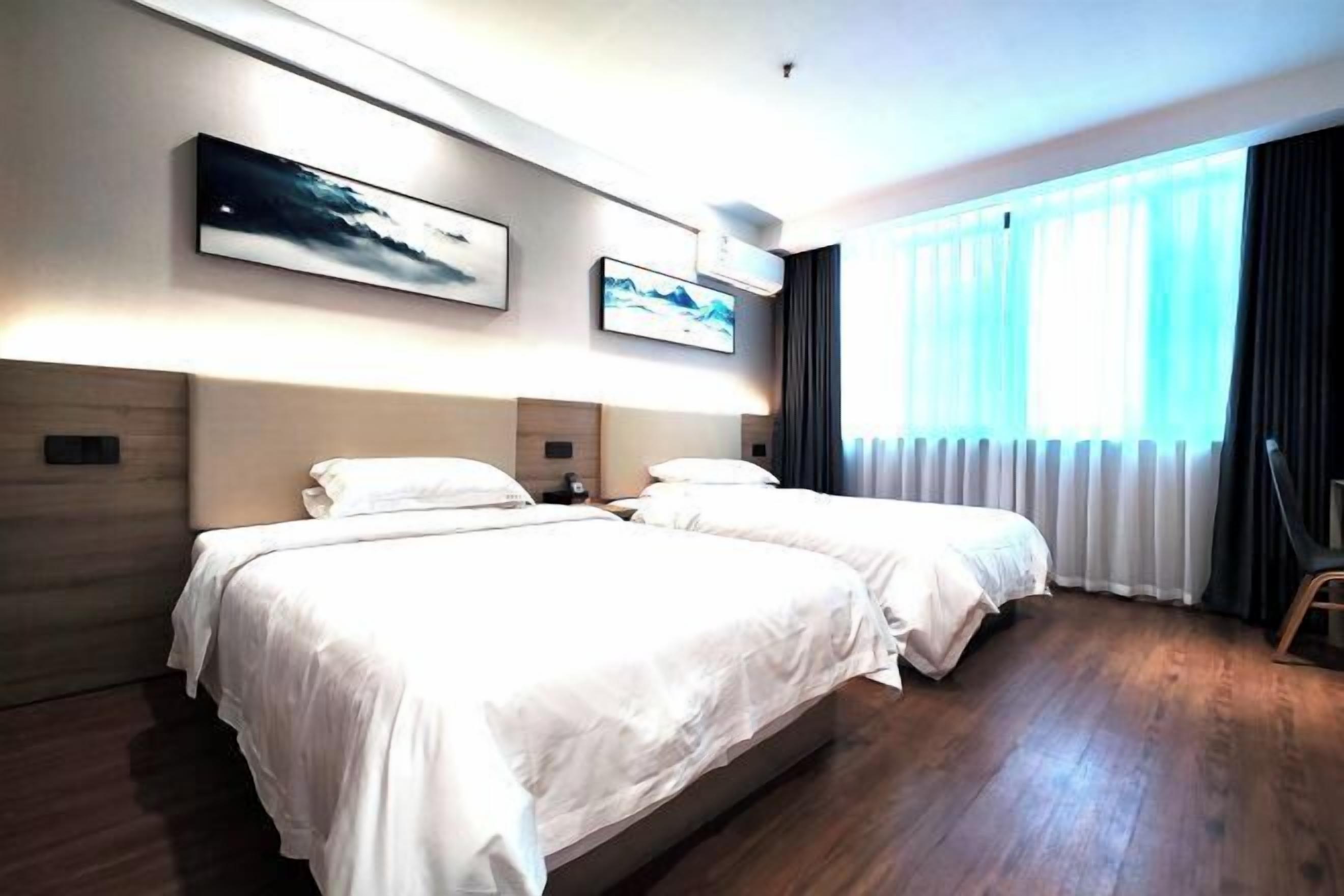 Quarto de hotel com duas camas, uma janela grande com cortinas e uma obra de arte na parede.