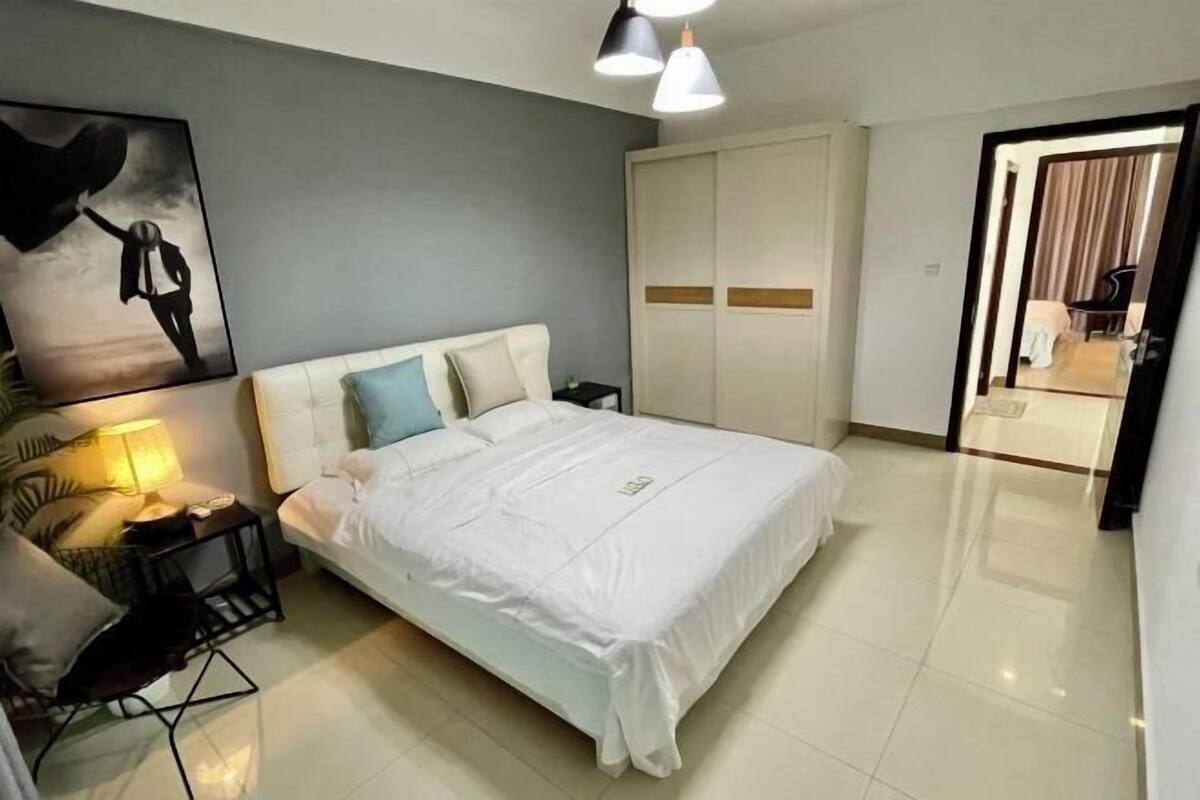 Um quarto com cama, mesas de cabeceira, abajur, quadro e guarda-roupa.
