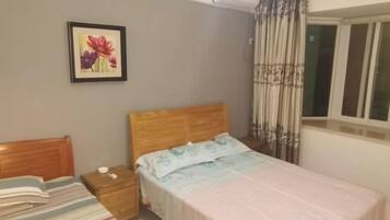 Quarto com cama, mesa de cabeceira, cortinas na janela e um quadro na parede.