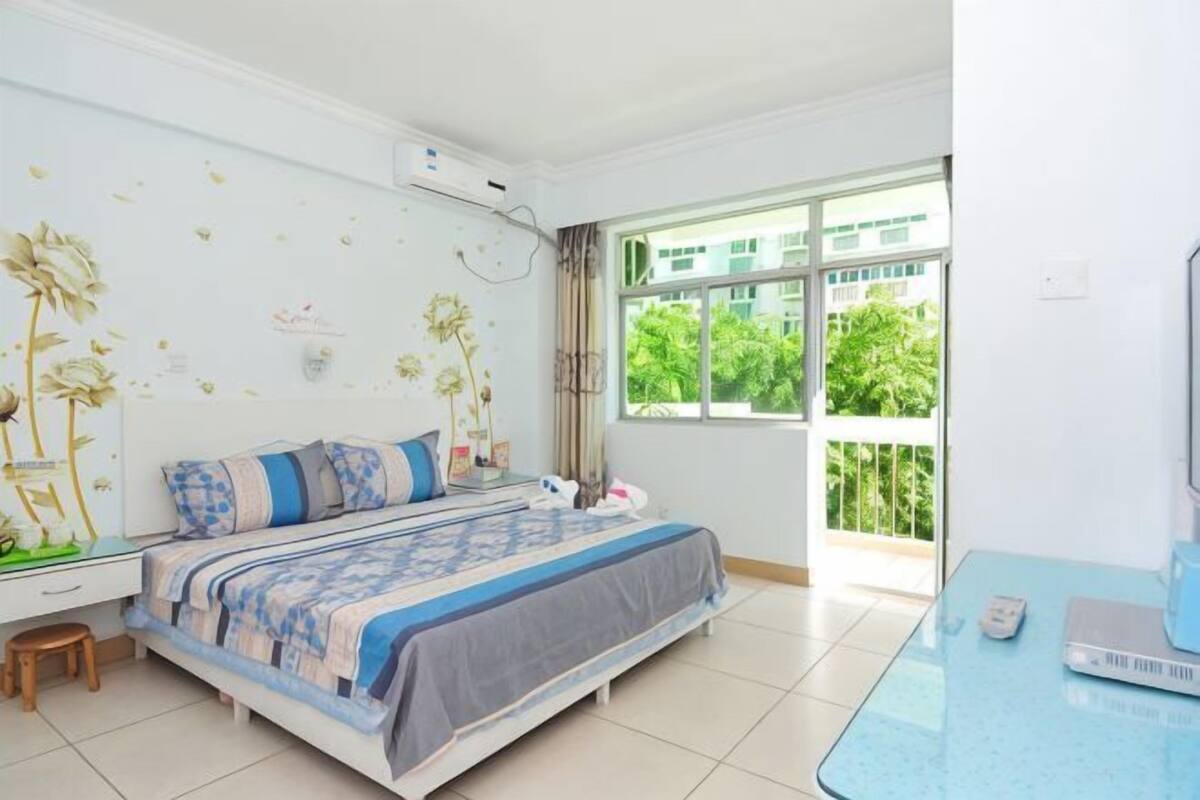 Quarto com cama, mesa de cabeceira e janela com vista para o verde.