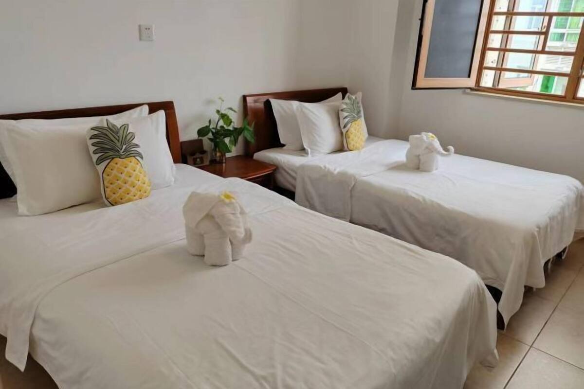 Quarto de hotel com duas camas, cada uma com um travesseiro de abacaxi e uma toalha com desenho de elefante.