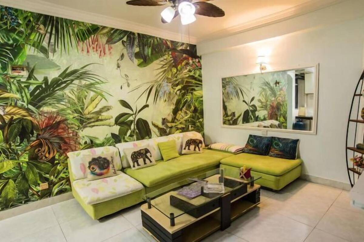 Uma sala de estar com um sofá verde, uma mesa de centro e um mural com folhagem tropical.