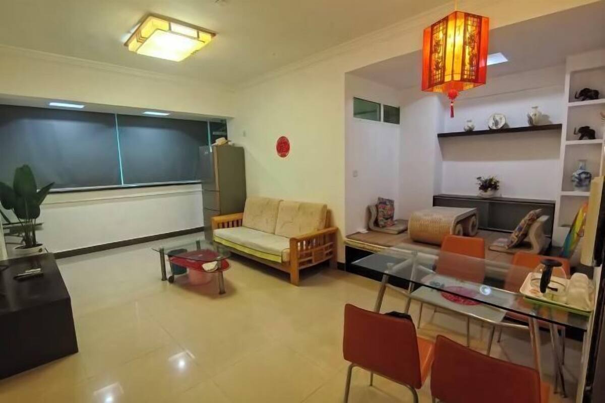 Uma sala de estar com sofá, cadeiras, mesa, televisão e um candeeiro vermelho.
