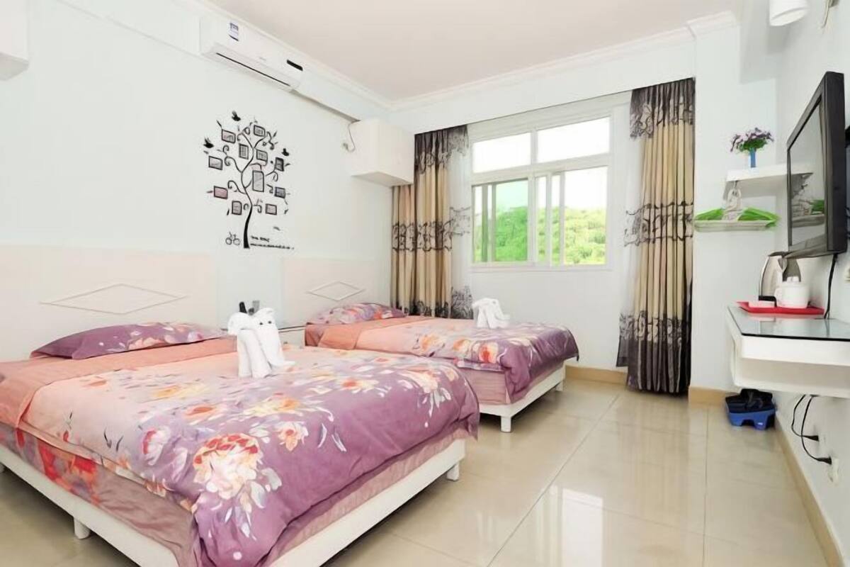 Quarto de hotel com duas camas, televisão, escrivaninha e janela com cortinas.