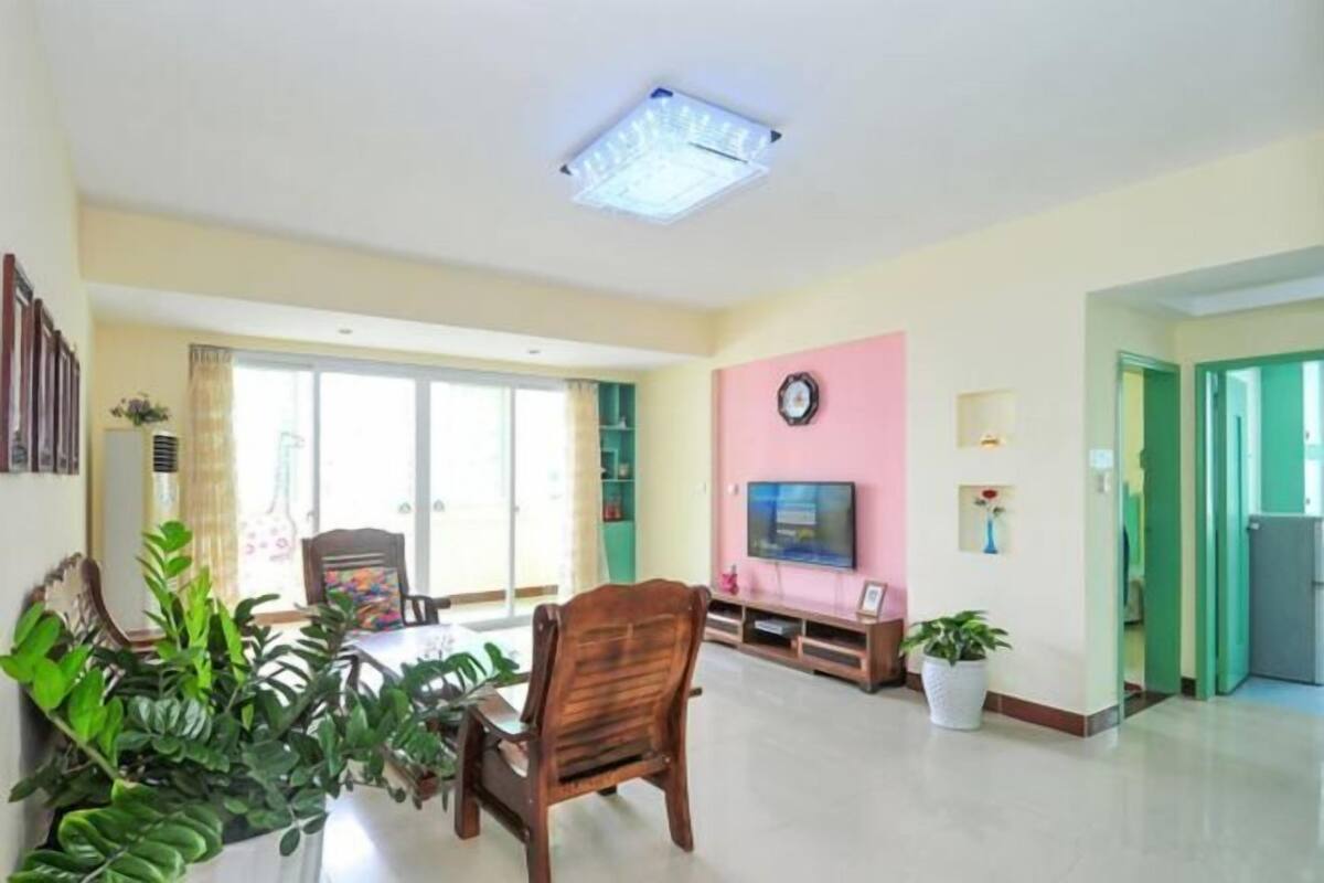 Uma sala de estar com televisão, uma cadeira de madeira, uma mesa de jantar e um vaso com planta.