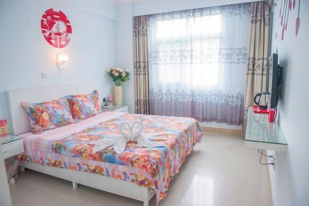 Quarto com cama, mesa de cabeceira, televisão e janela com cortinas.