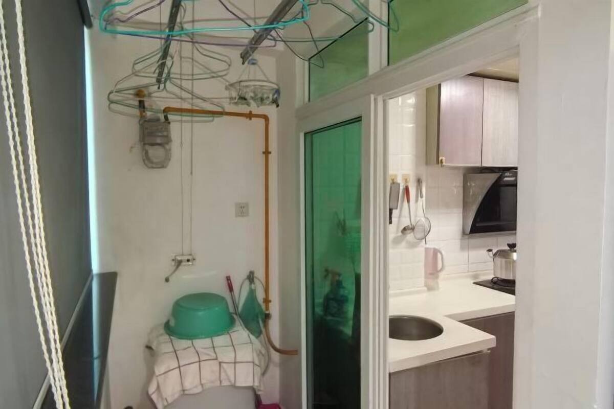 Um corredor estreito que dá para um banheiro com porta verde, pia e vaso sanitário.